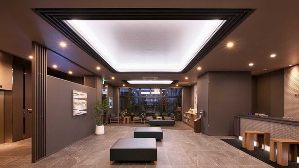 Um hall moderno com claraboia, área de estar, balcão de recepção e vista para o exterior.