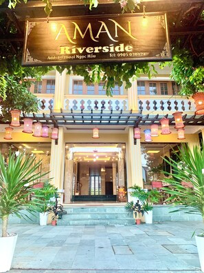 Entrada de hotel com uma placa indicando "AMAN Riverside" e um número de contato.