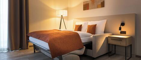 Quarto de hotel moderno com cama, mesa de cabeceira, abajur e obra de arte na parede.