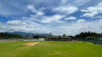 Um amplo campo gramado com um campo de beisebol, cercado por uma cerca e árvores.