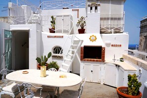 Um edifício branco com um pátio que inclui uma mesa redonda, cadeiras e plantas em vasos.