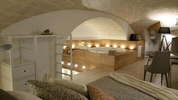 Quarto com uma cama grande, penteadeira de madeira com banheira, e escrivaninha com cadeira.