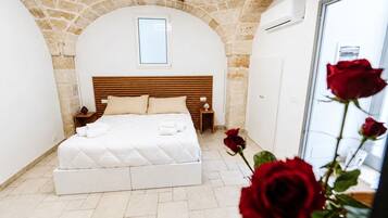 Quarto com teto em arco de pedra, cabeceira de madeira, cama com roupa de cama branca, mesa de cabeceira e janela.