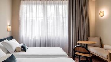 Quarto de hotel com duas camas, uma mesinha redonda, um sofá e uma cadeira.