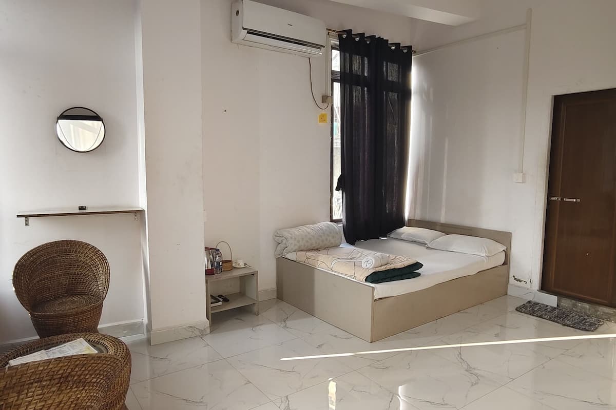 Um quarto com cama, poltrona, mesa de cabeceira e guarda-roupa.