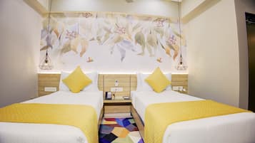 Quarto de hotel com duas camas, um tapete geométrico colorido, um mural floral na parede e um ventilador de teto.