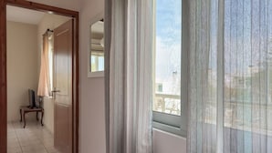 Um corredor com porta de madeira, uma cadeira e uma janela com cortinas.