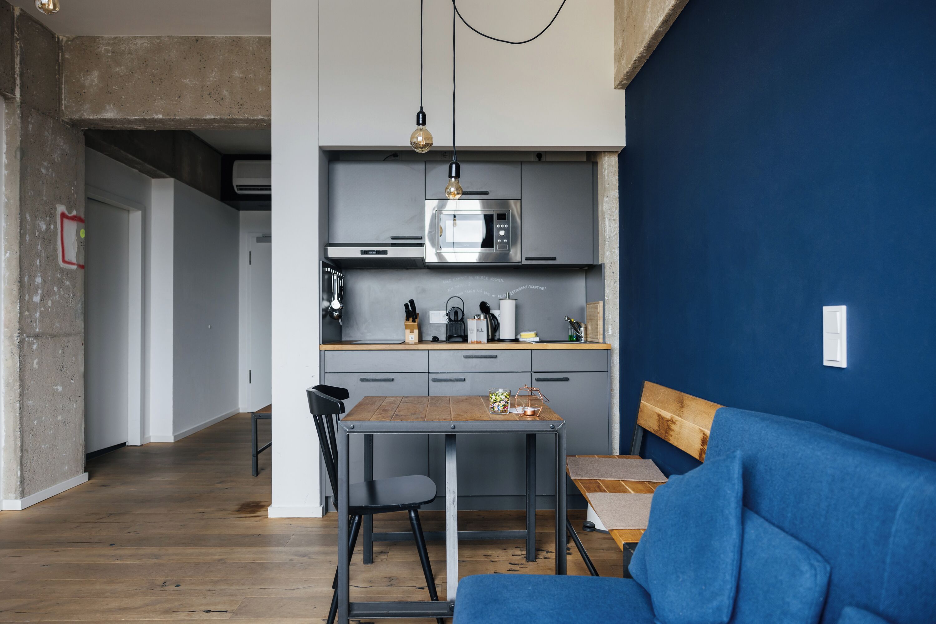 Cozinha moderna com micro-ondas, mesa de jantar, cadeiras e um sofá azul.