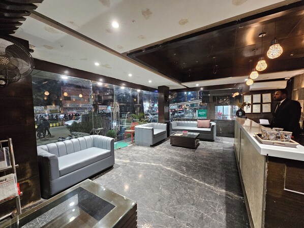 Um saguão moderno com sofás de couro, uma mesa de centro de vidro e um balcão de recepção com um homem atrás.