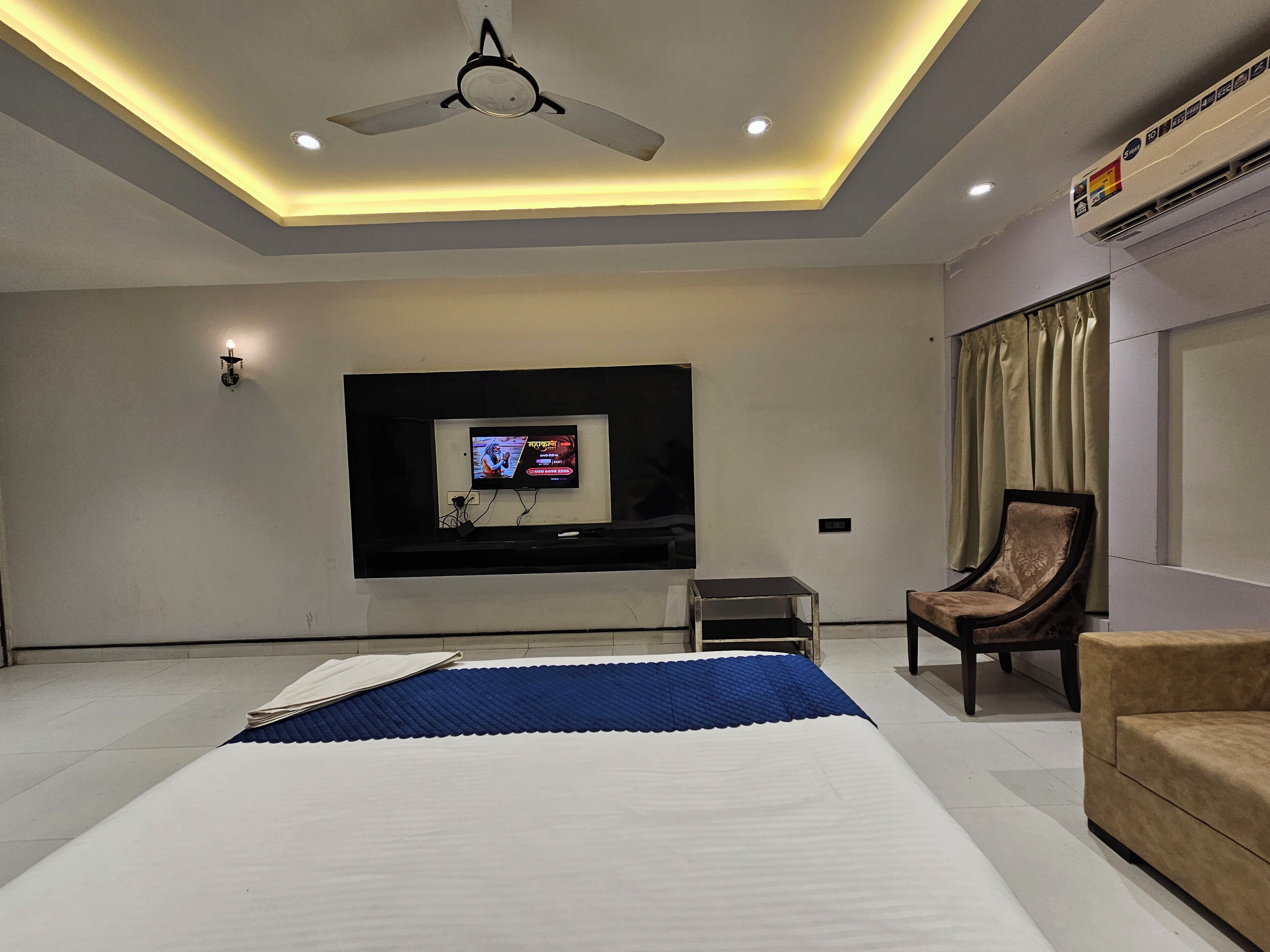 Quarto moderno com cama, TV fixada na parede, ventilador de teto e janela com cortinas.