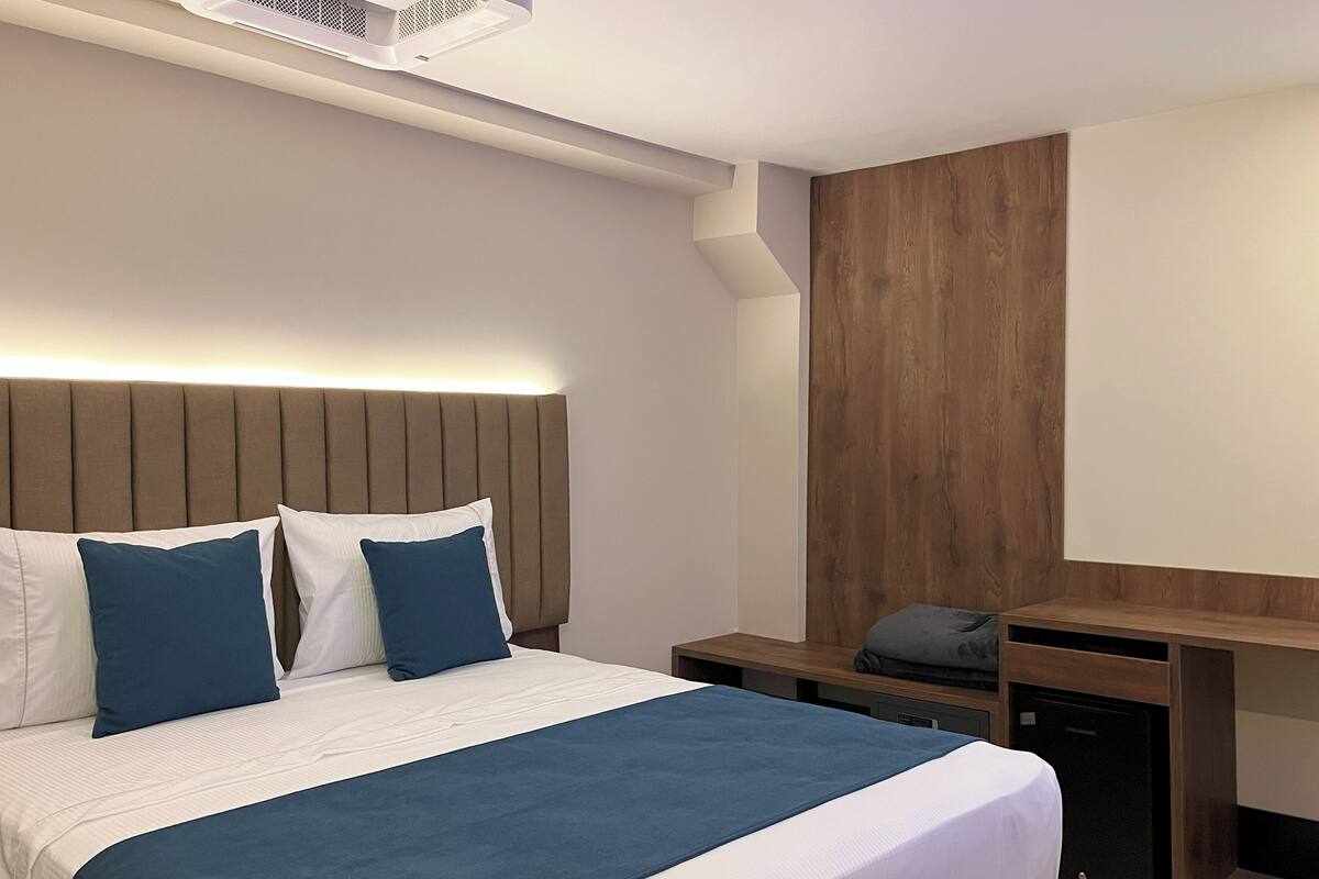 Quarto de hotel moderno com uma cama grande, cabeceira de madeira, uma escrivaninha e aquecedor embutido.