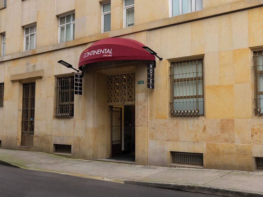 Entrada de um hotel com toldo cor de vinho, uma placa indicando o nome 'Continental Hotel' e o número '4-25' na porta.