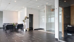 Um hall moderno com chão de azulejos escuros, área de estar com cadeiras pretas, divisória de vidro e lareira.
