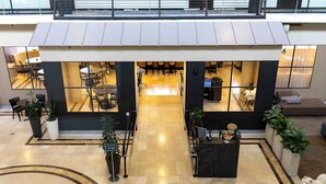 Um lobby de hotel moderno com uma escadaria central, áreas de estar e um balcão de recepção.