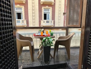 Uma varanda com duas cadeiras de vime, uma mesinha com bandeja e um vaso de planta.