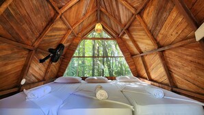 Um quarto acolhedor com teto de madeira, uma cama, um ventilador e uma janela com vista para vegetação exuberante.