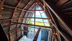 Quarto com teto alto, vigas de madeira e uma grande janela com vista para o exterior.