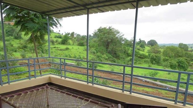 Uma varanda coberta com uma rede e uma cadeira, com vista para uma paisagem verde exuberante.