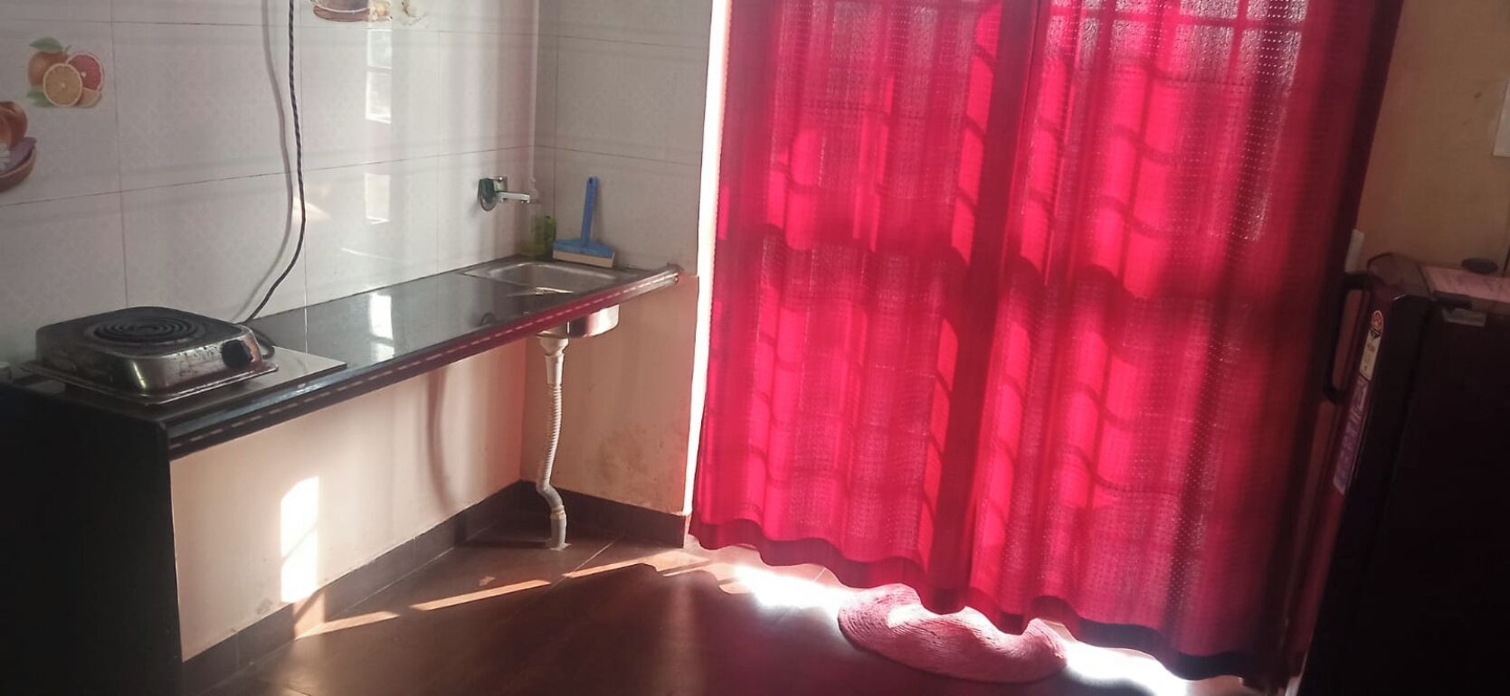 Uma cozinha com fogão a gás, pia e cortina vermelha.