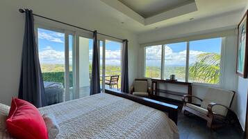 Quarto com uma cama grande, uma escrivaninha e uma cadeira, com vista para a paisagem pelas janelas.