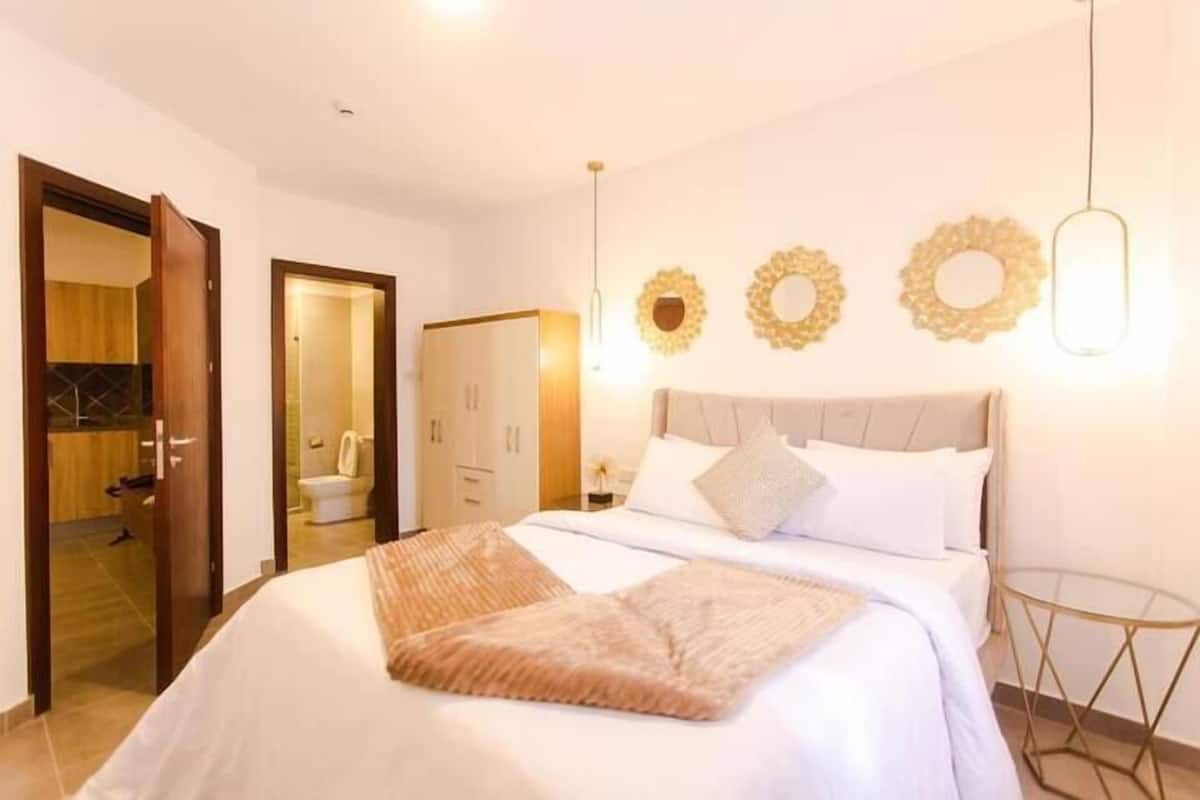Quarto de hotel com cama, mesa de cabeceira, espelho redondo e guarda-roupa.