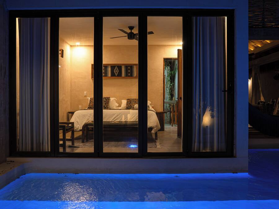 Quarto de hotel moderno com uma grande porta de vidro deslizante, uma cama, ventoinha no teto e área com hidromassagem.