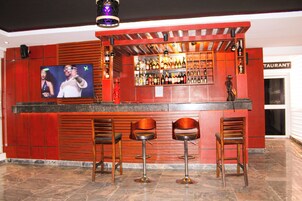 Uma área de bar com uma tela de televisão, um suporte para vinhos e três banquetas.