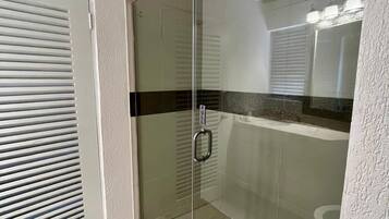 Um chuveiro com paredes de vidro, uma toalha pendurada na parede, uma porta com puxador e chão revestido de azulejos.