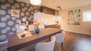 Cozinha moderna com mesa de jantar de madeira, duas cadeiras, um vaso com flores e um candeeiro fixado na parede.