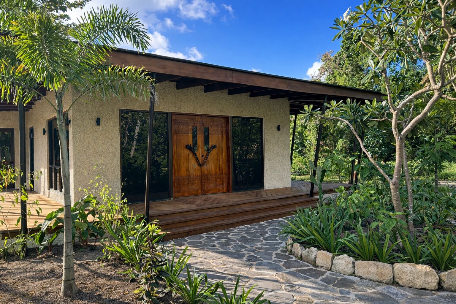 Uma casa moderna com um caminho de pedra que leva a uma porta de madeira, cercada por vegetação exuberante.