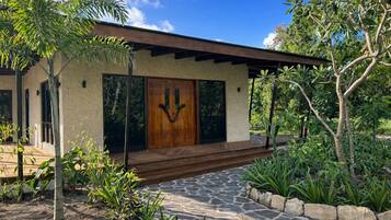 Uma casa moderna com um caminho de pedra que leva a uma porta de madeira, cercada por vegetação exuberante.