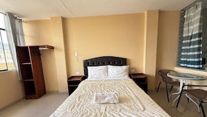 Quarto de hotel com cama, guarda-roupa, uma pequena mesa e uma cadeira.