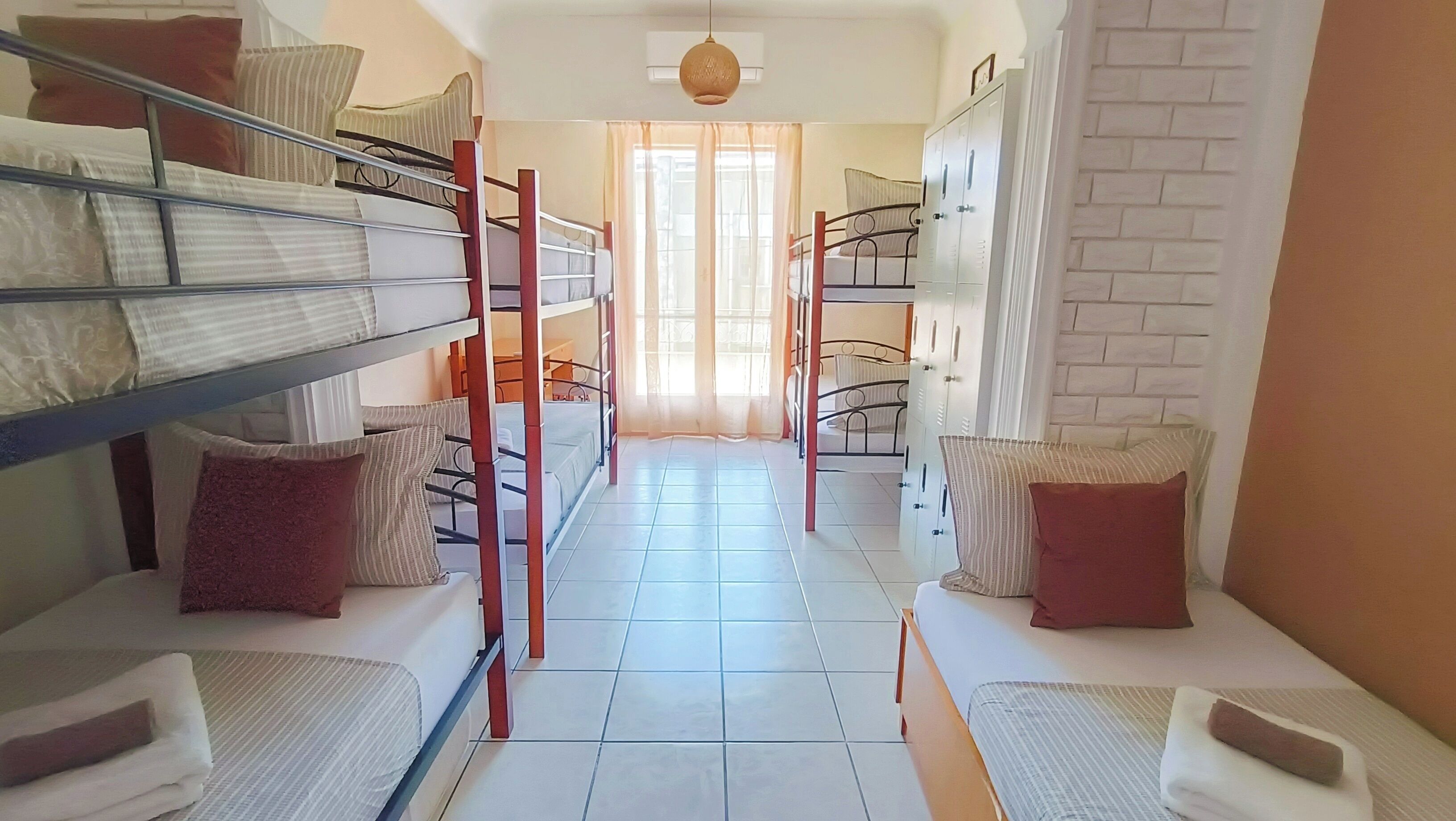 Um quarto de dormitório com beliches, piso de azulejos e janela com cortinas leves.