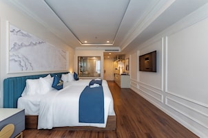 Quarto de hotel com uma cama grande, uma escrivaninha, uma televisão e um banheiro visível por uma porta aberta.