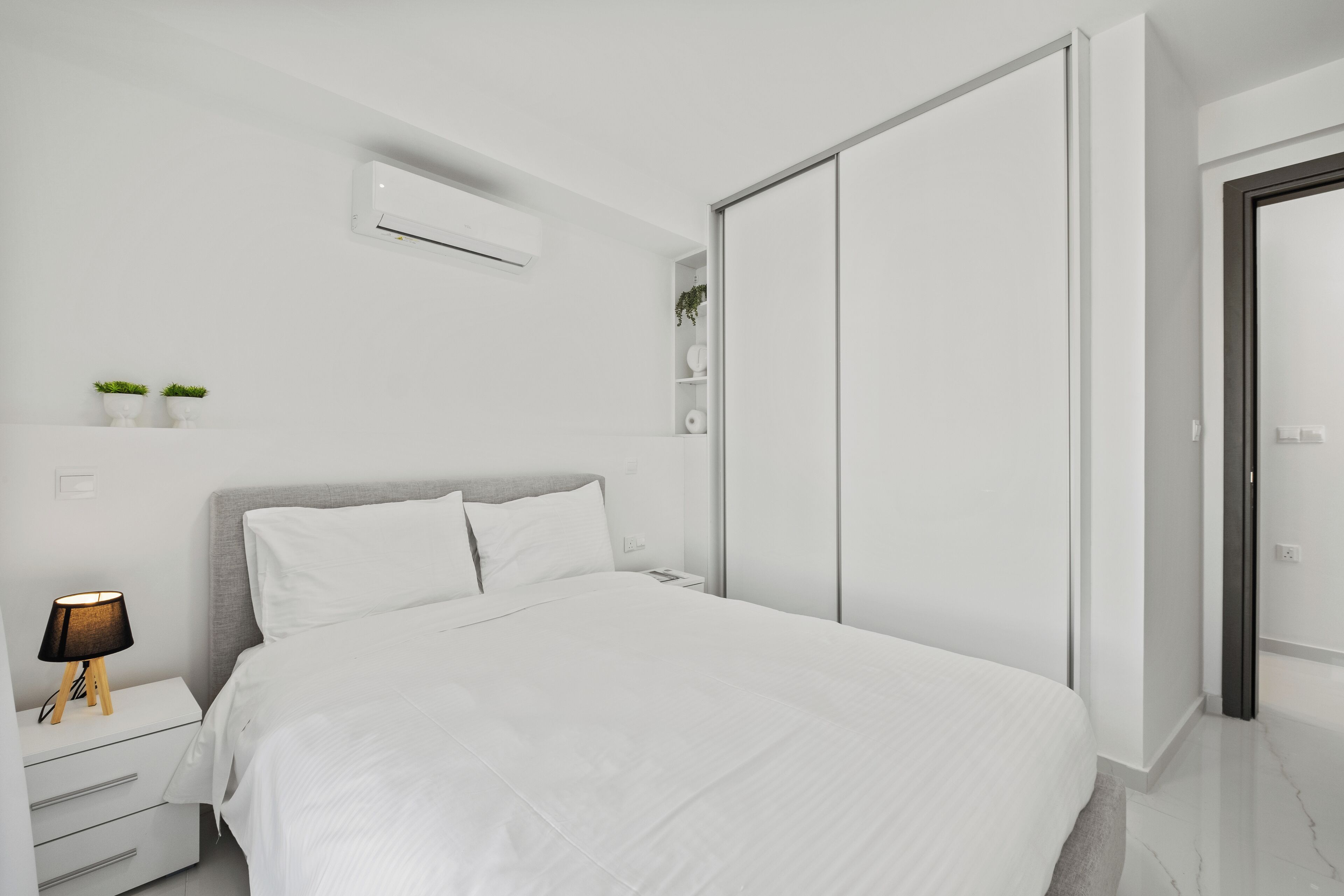 Quarto moderno com cama, mesa de cabeceira, luminária, aparelho de ar condicionado e guarda-roupa.