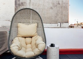 Uma cadeira suspensa com almofada e uma pequena mesa com uma xícara em um terraço.