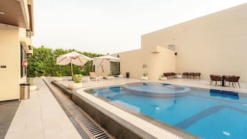 Uma piscina com espreguiçadeiras e guarda-sóis, rodeada por um edifício com chão de azulejos e uma lixeira.