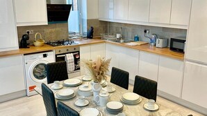 Cozinha moderna com ilha central, eletrodomésticos embutidos e área de jantar com mesa posta para quatro.