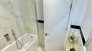 Um banheiro moderno com box de vidro, uma banheira branca e uma porta com faixa preta.