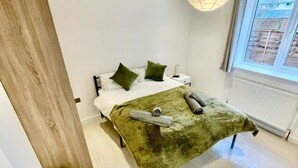 Quarto com cama, almofadas e manta verdes, e uma toalha enrolada sobre a cama.
