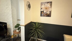 Quarto com lareira de tijolos brancos, parede com detalhes em preto e branco, uma grande planta em vaso e uma obra de arte floral emoldurada.