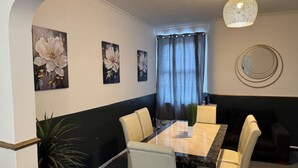 Uma sala de jantar com mesa de mármore, cadeiras brancas e obras de arte com motivos florais nas paredes.