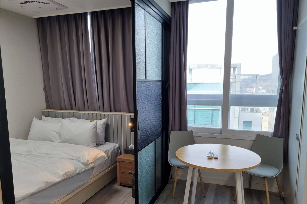 Quarto de hotel com cama, mesa de cabeceira e pequena mesa redonda com cadeiras.