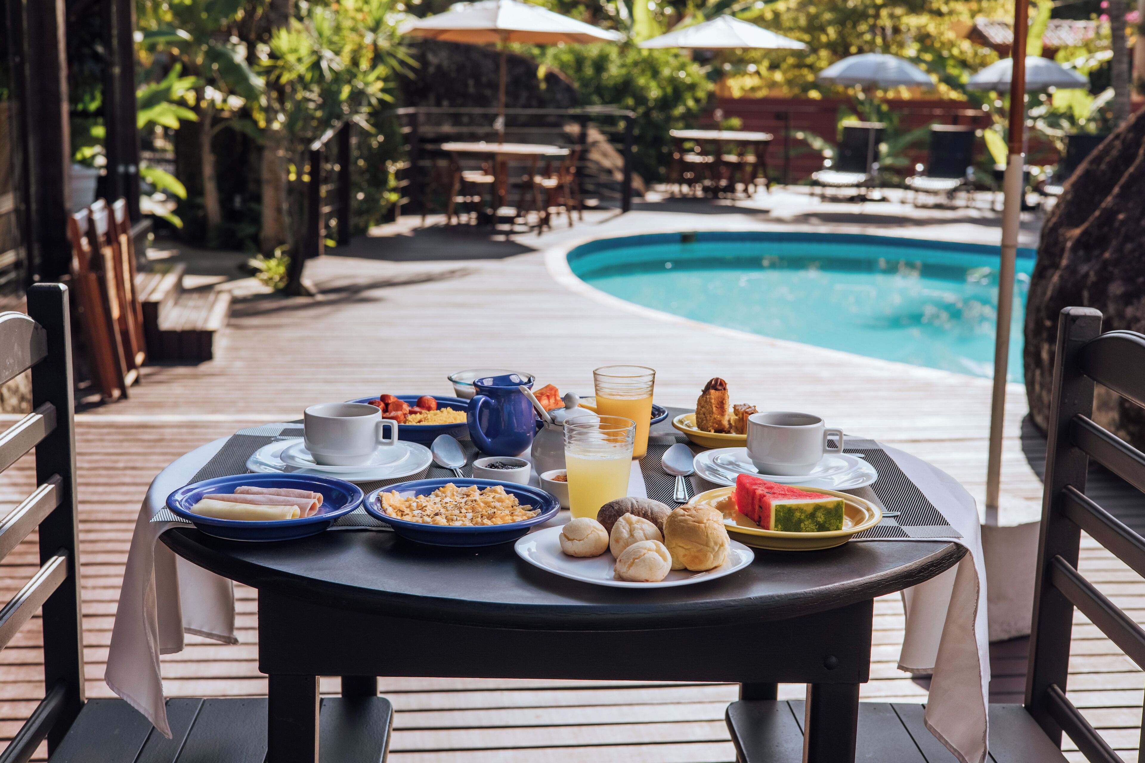 Mesa de jantar com itens de café da manhã e piscina ao fundo.