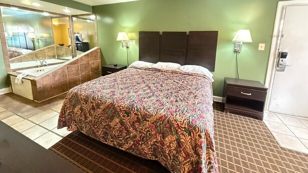 Quarto de hotel com uma cama grande, banheiro com banheira e um espelho.