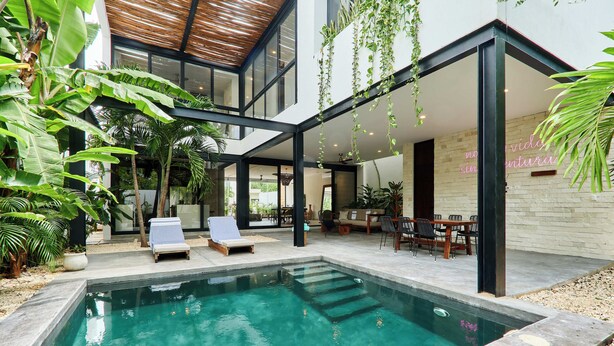 Uma área de piscina moderna ao ar livre, com espreguiçadeiras, espaço para refeições e vegetação exuberante.