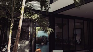 Uma área de estar ao ar livre moderna, com piscina, palmeiras e um terraço envidraçado.