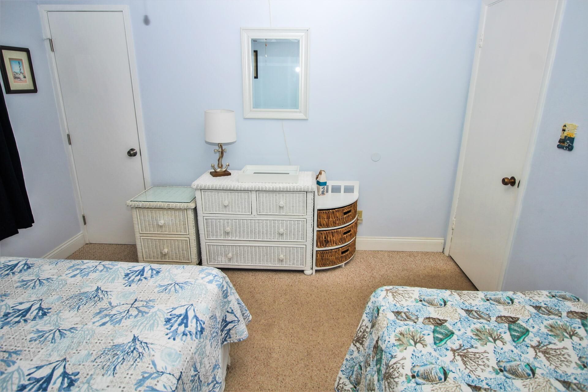 Quarto com duas camas, cômoda, abajur e espelho na parede.