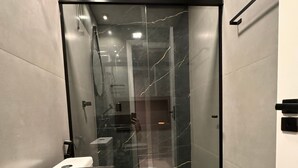 Um banheiro moderno com box de vidro, pia de mármore preto e vaso sanitário branco.