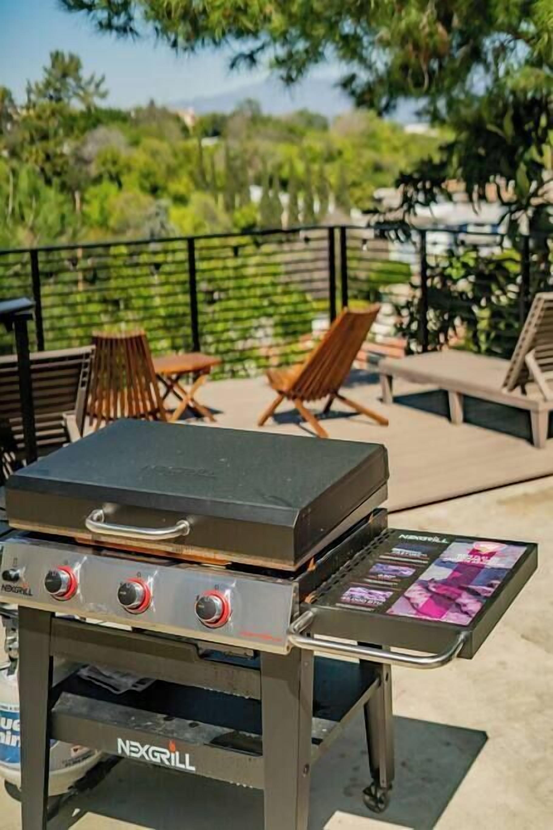 Uma churrasqueira NEXGRILL com carrinho, área de estar externa e vista para um lago.